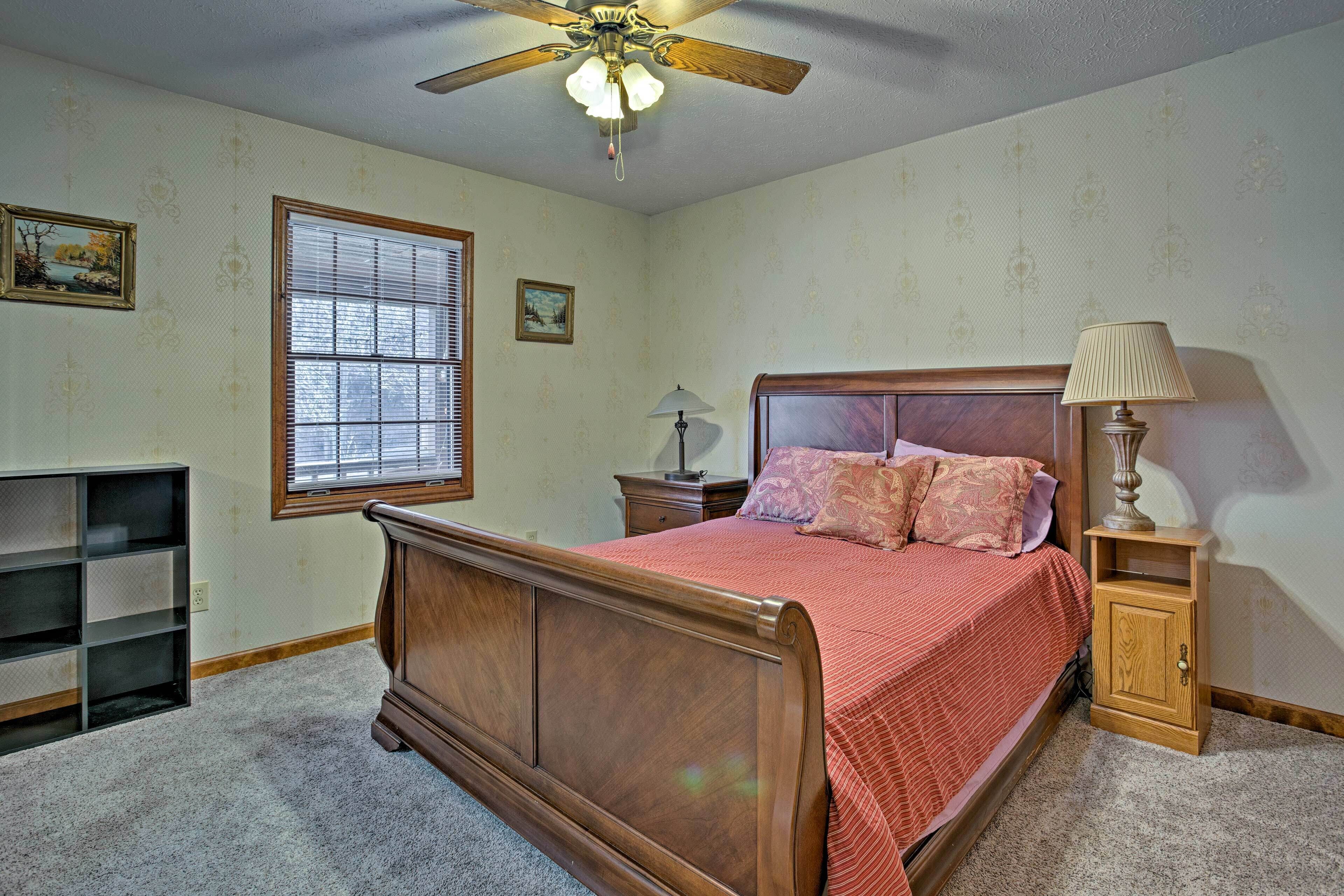 Um quarto com cama de madeira, mesa de cabeceira, luminária, janela com persianas e estante de livros.