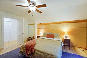Quarto com cama, abajures, cabeceira de madeira, ventilador de teto e uma porta.