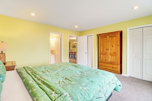 Quarto com uma cama grande, um guarda-roupa de madeira e uma porta que dá para outro cômodo.