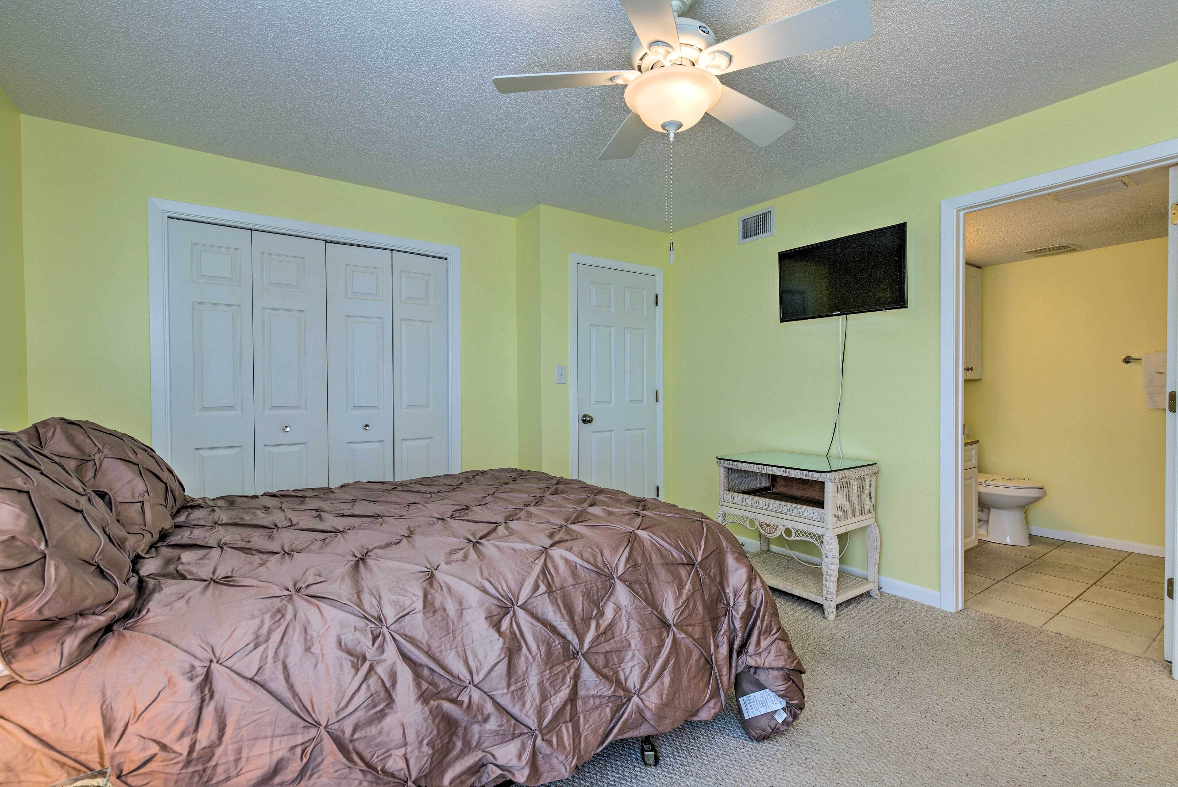 Quarto com cama, ventilador de teto e porta para um banheiro.