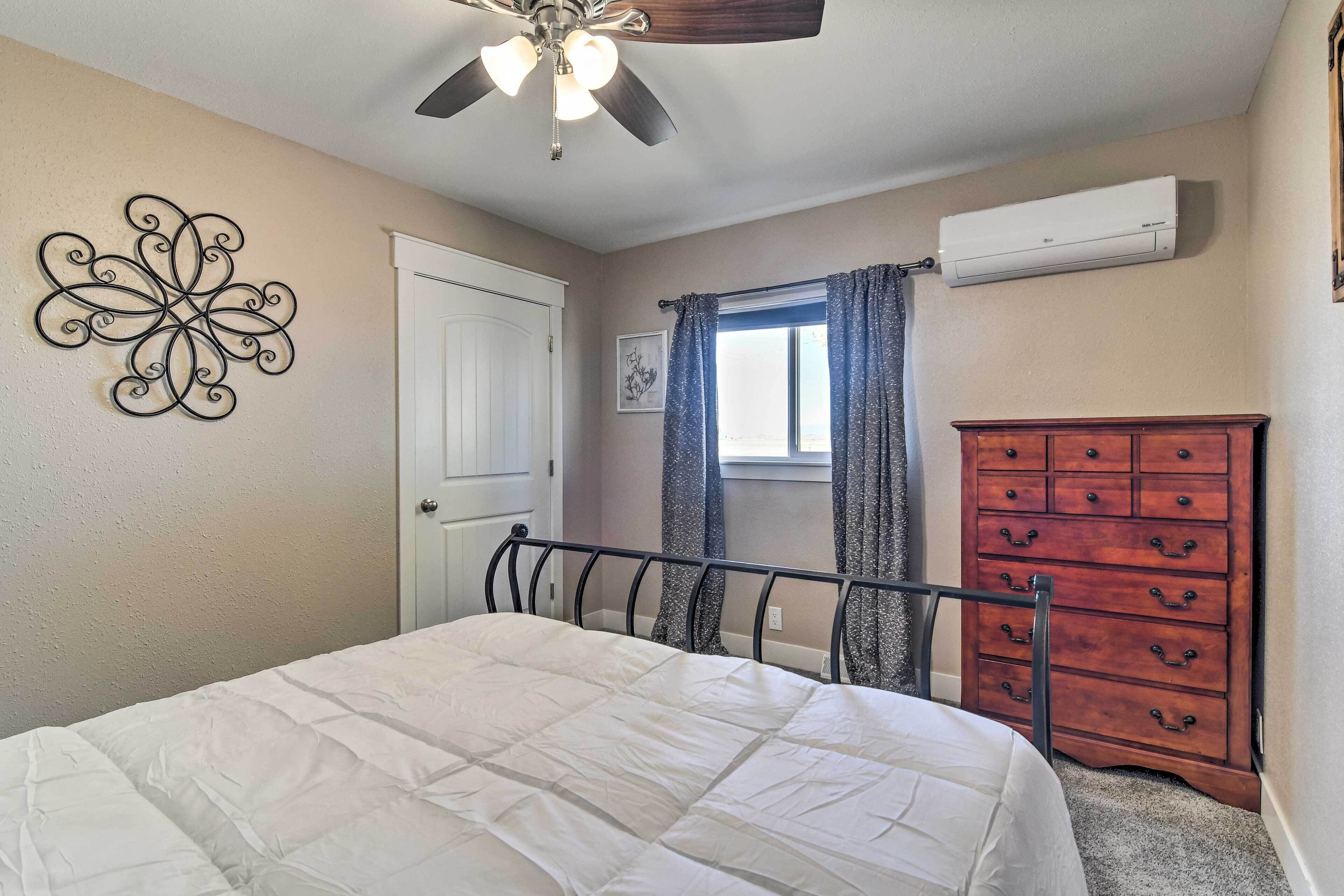 Quarto com cama, penteadeira, ventilador de teto e janela com cortinas.