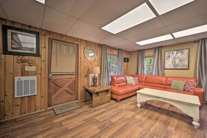 Um quarto acolhedor com porta de madeira, um sofá de couro vermelho, uma mesa de centro de madeira e um relógio de parede.
