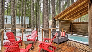 Um deck de madeira com cadeiras Adirondack vermelhas, um sofá cinza e uma banheira de hidromassagem.