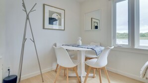 Uma área de refeições com mesa branca, duas cadeiras brancas, um jogo americano azul e quadros nas paredes.