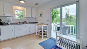 Uma cozinha moderna com armários brancos, forno embutido e janela com vista para um deck.