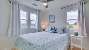 Quarto com cama, duas janelas, ventilador de teto, mesa de cabeceira e luminária.