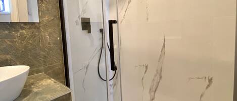 Uma casa de banho moderna com chuveiro em cabine de vidro, paredes de mármore e lavatório branco.