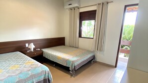 Quarto com duas camas, janela com cortinas, ventilador de teto e ar condicionado.