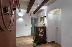 Uma área de recepção com piso de madeira, balcão de atendimento e porta de vidro que dá para um salão.