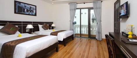 Quarto de hotel com duas camas, uma escrivaninha, televisão e varanda com cortinas.