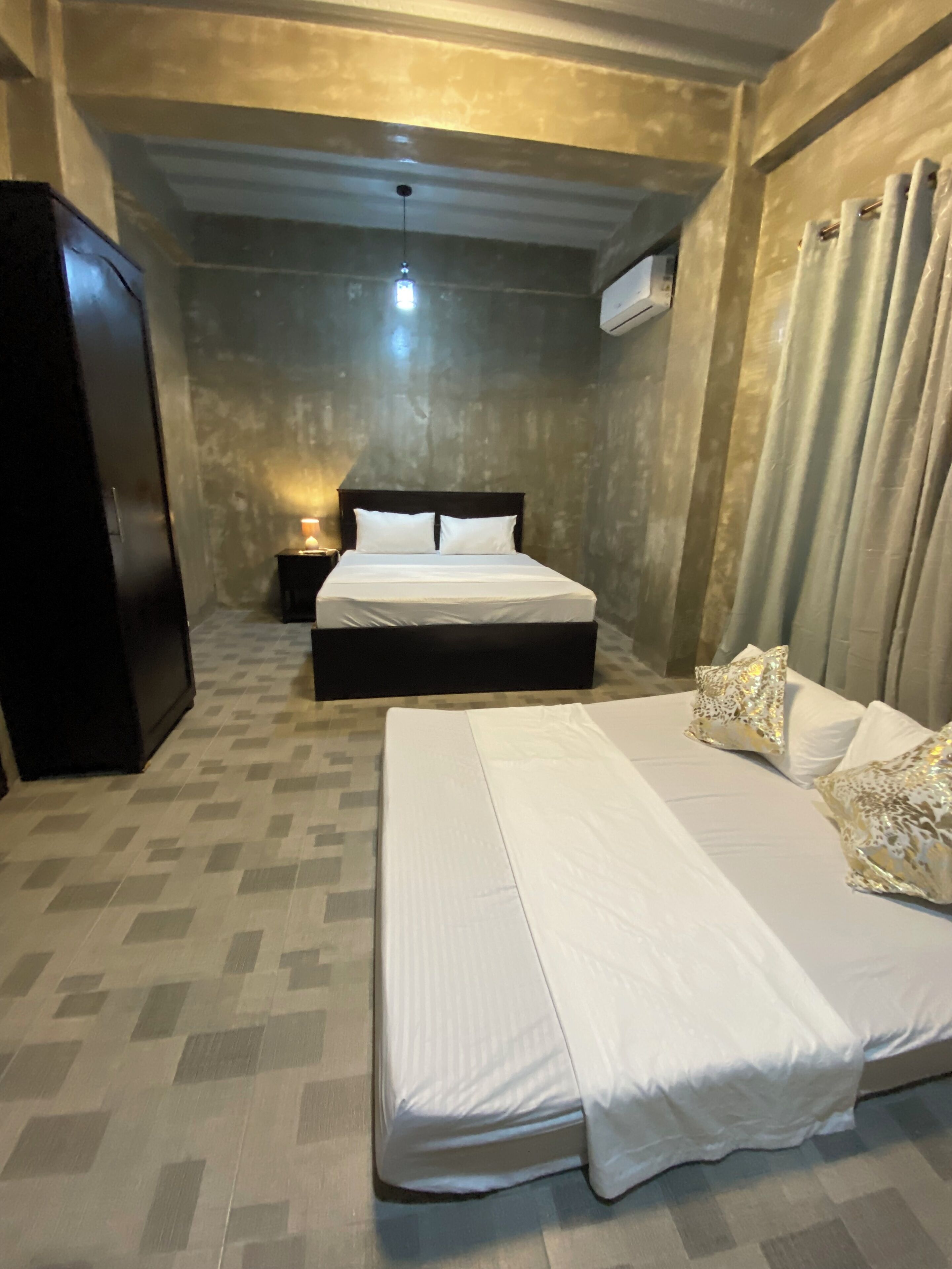 Um quarto com uma cama grande, uma cama menor, uma mesa de cabeceira, um guarda-roupa e uma luminária no teto.