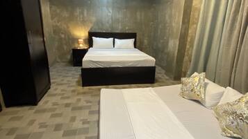 Um quarto com uma cama grande, uma cama menor, uma mesa de cabeceira, um guarda-roupa e uma luminária no teto.