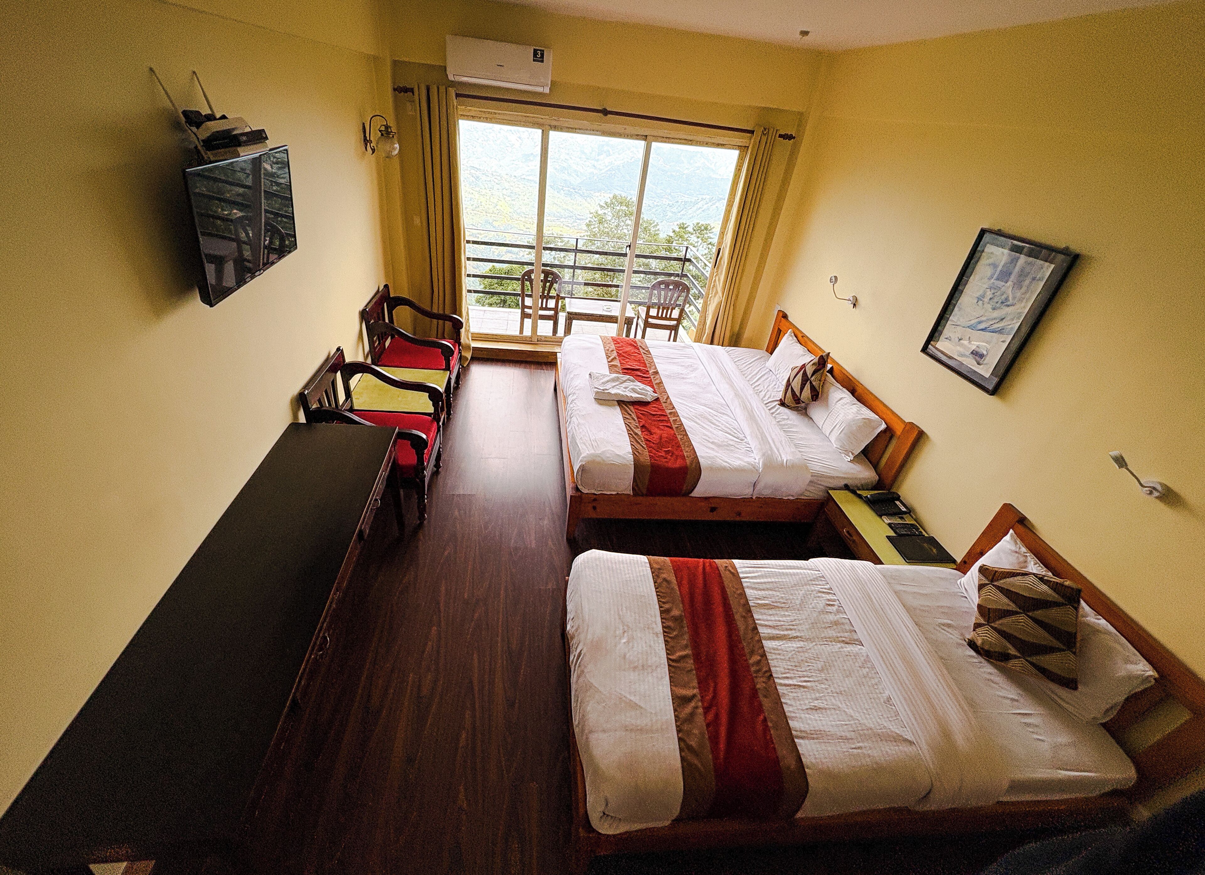 Quarto de hotel com duas camas, uma mesa, uma cadeira e janela com vista.