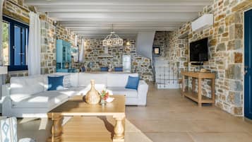 Uma sala de estar ampla com parede de pedra, um sofá branco, uma mesa de centro de madeira e uma televisão na parede.