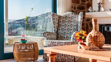 Uma sala de estar acolhedora com uma poltrona estampada, uma mesa de madeira e uma mesinha de vime com uma tigela de frutas.