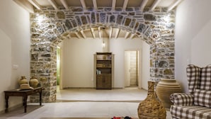 Uma arcada de pedra que dá acesso a um quarto com chão de madeira, uma estante e um sofá xadrez.