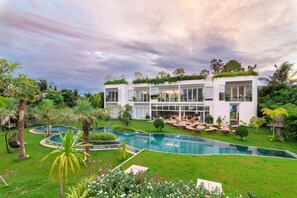 Uma casa moderna com dois andares, piscina, cercada por vegetação exuberante e palmeiras.