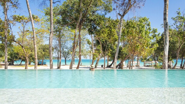 Piscina azul límpida rodeada por árvores e uma praia de areia.