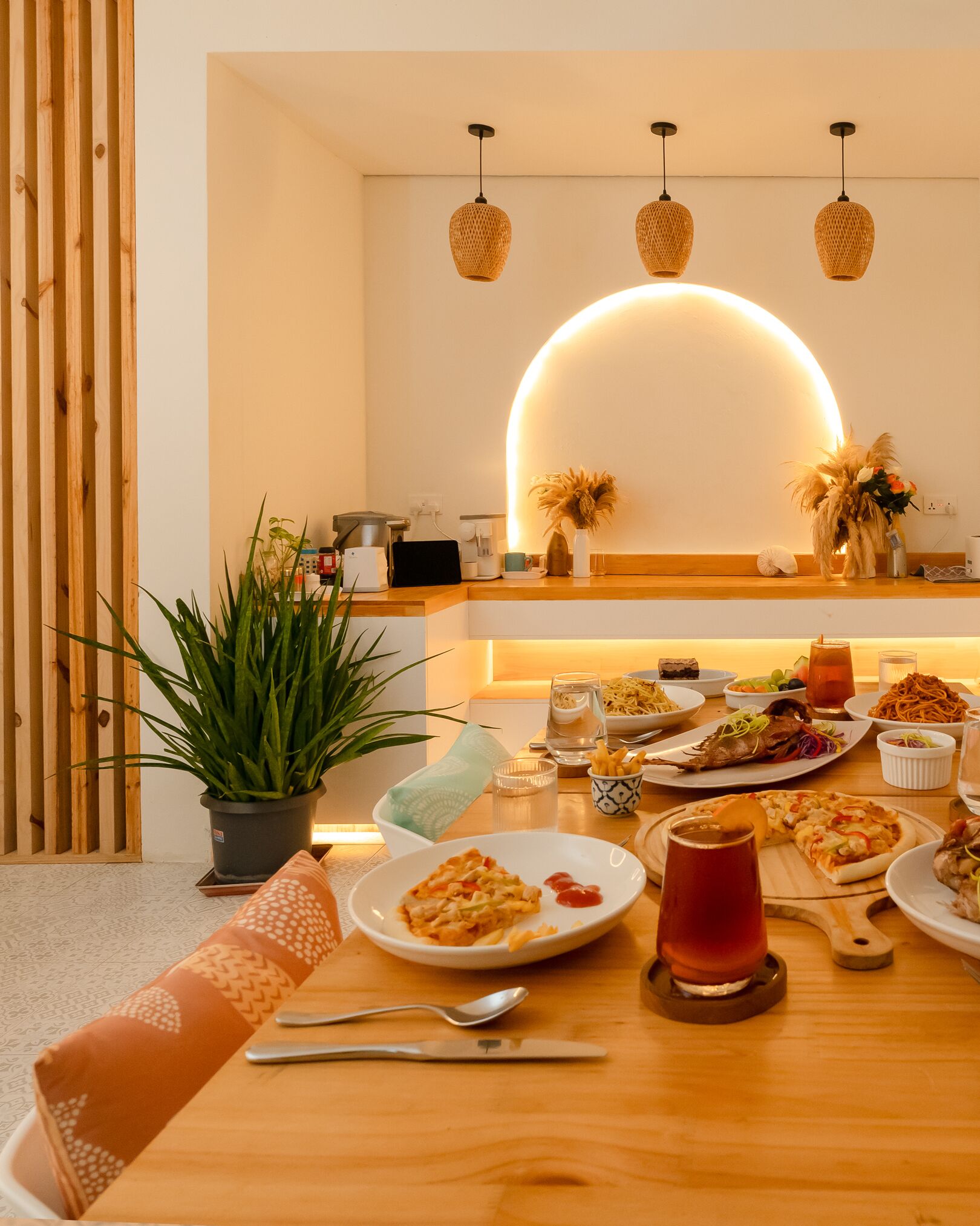 Uma área de refeições com uma mesa de madeira posta para uma refeição, uma planta em vaso e um cão no balcão.