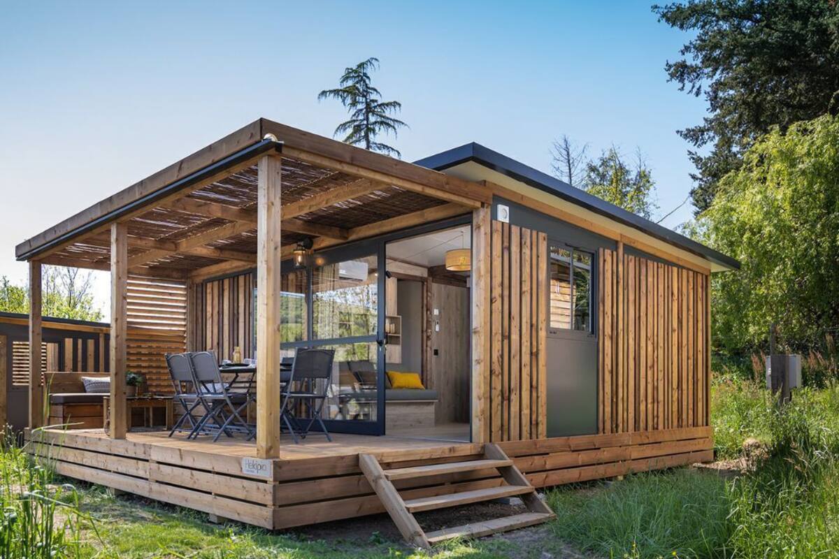 Uma cabana de madeira moderna com varanda coberta, área de refeições e espaço para dormir.