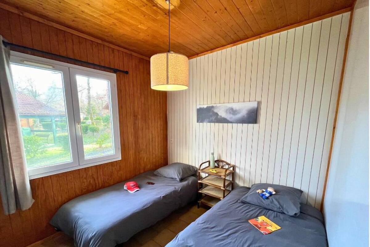 Quarto com duas camas de solteiro, teto de madeira, janela com vista para o verde e um quadro pendurado na parede.