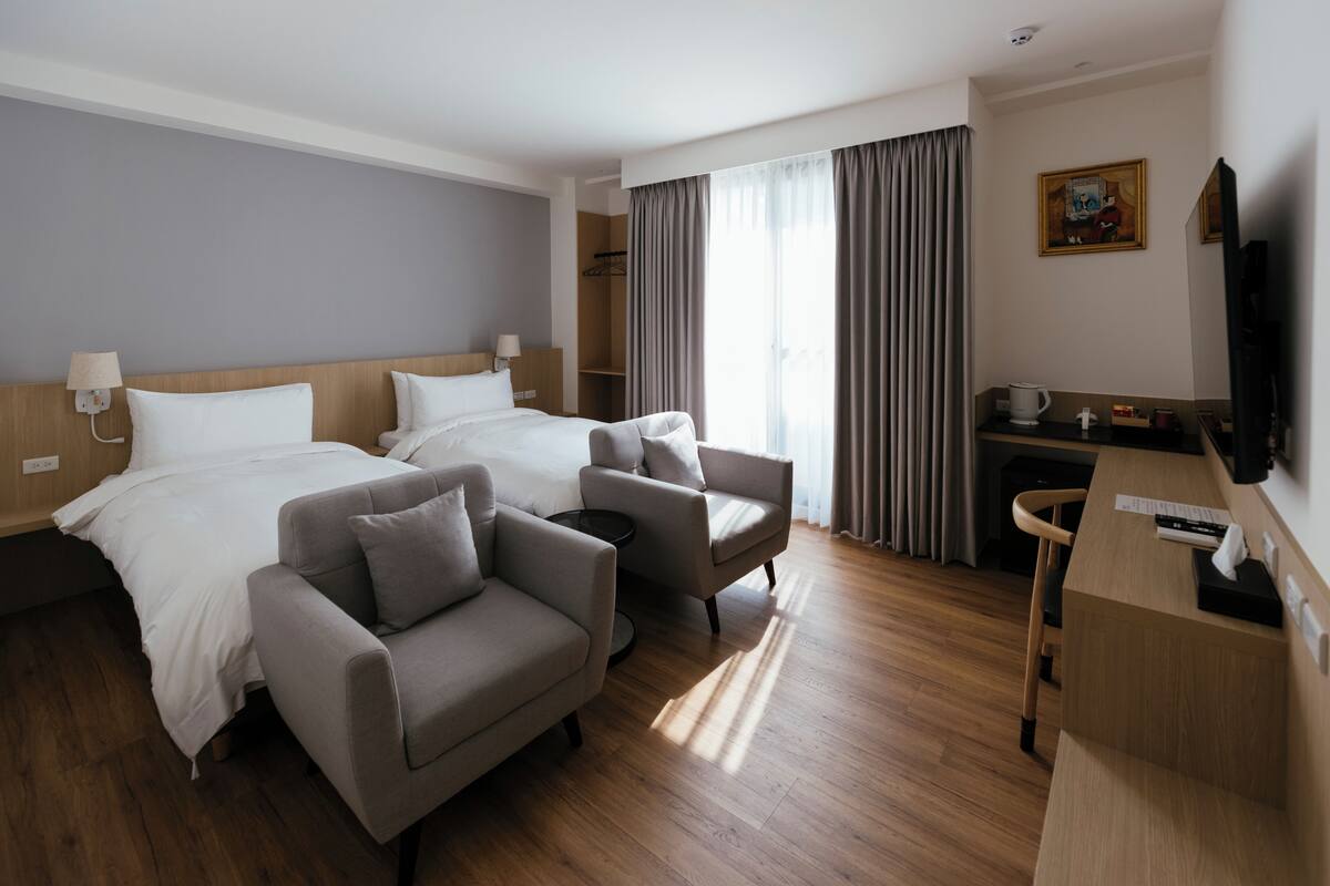 Quarto de hotel com duas camas, um sofá, uma escrivaninha e uma televisão.