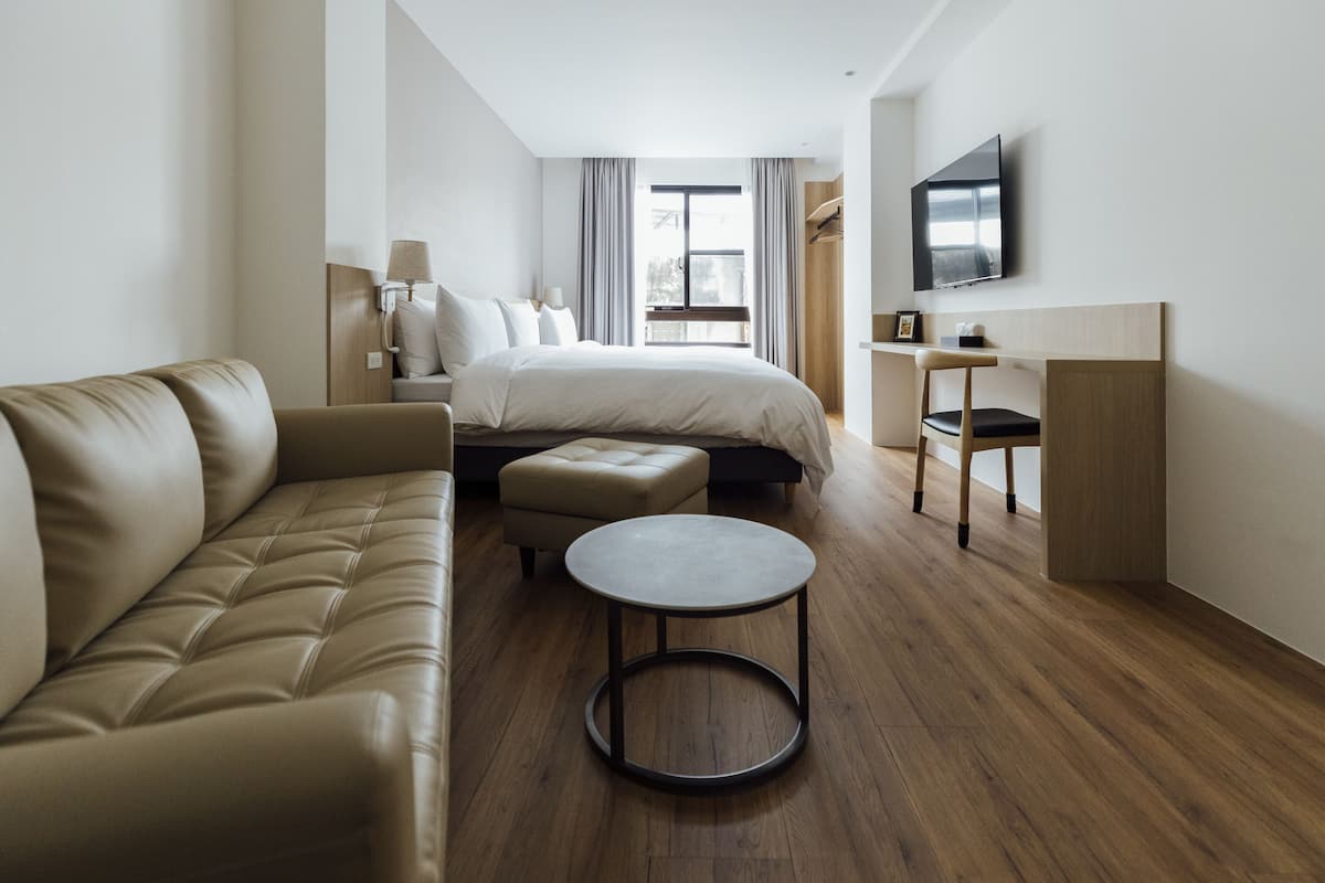 Quarto de hotel moderno com uma cama grande, um sofá, uma mesa redonda e uma televisão fixada na parede.