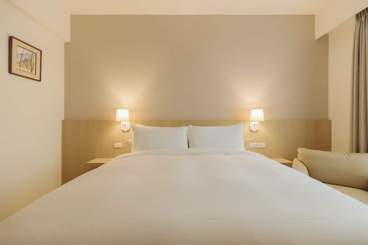 Quarto de hotel com uma cama grande, luminárias laterais, mesa de cabeceira e um quadro na parede.