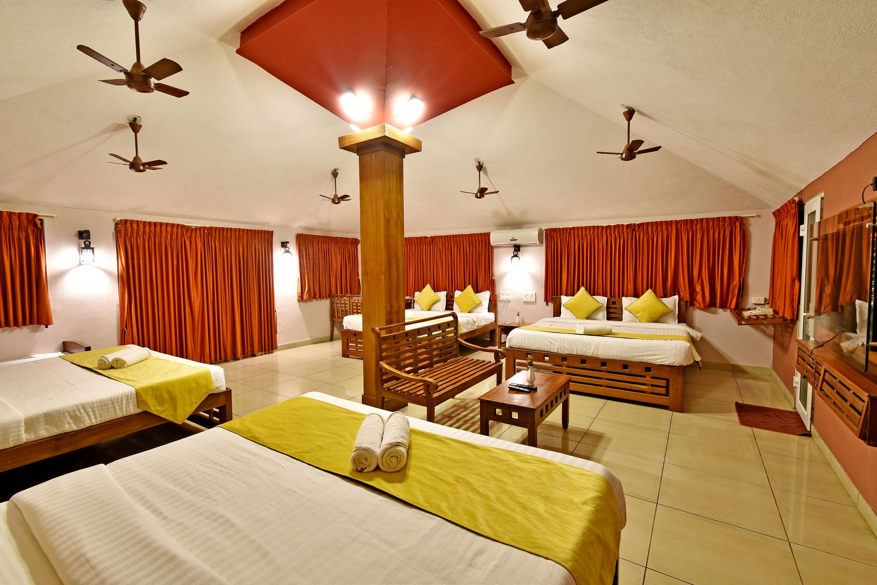 Quarto de hotel com quatro camas, móveis de madeira e ventiladores de teto.