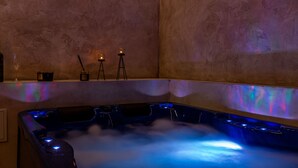 Banheira de hidromassagem com iluminação azul e vapor, cercada por uma parede texturizada e velas.