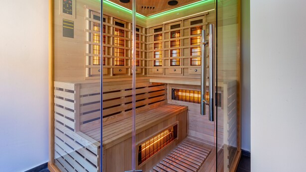 Uma sauna com bancos de madeira e paredes de vidro, incluindo um painel de controle e sistema de ventilação.