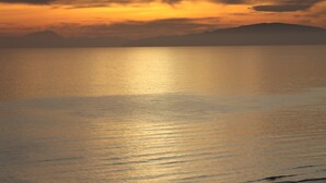 Mar calmo ao pôr do sol, com silhueta de montanhas ao fundo.