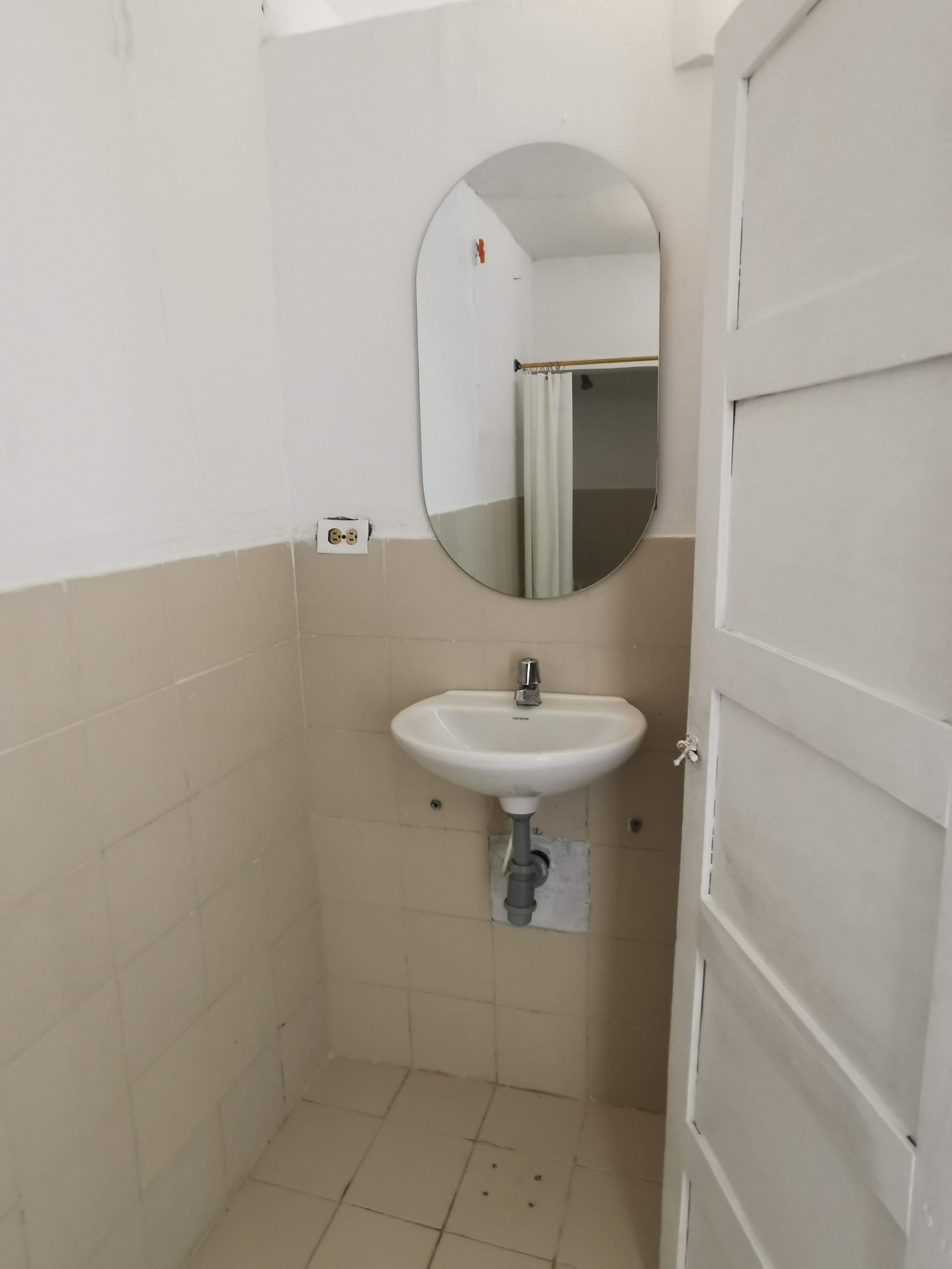 Uma casa de banho pequena com uma pia branca, um espelho redondo e uma porta branca.