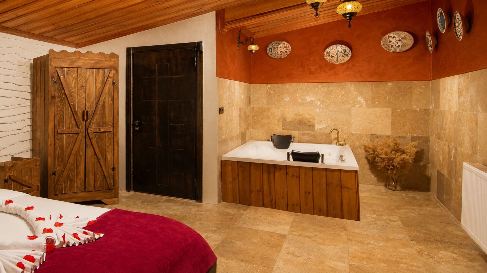 Quarto com porta de madeira, piaça branca e toalha preta, e manta vermelha na cama.