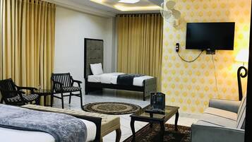 Quarto de hotel com cama, sofá, televisão, escrivaninha e cadeira.
