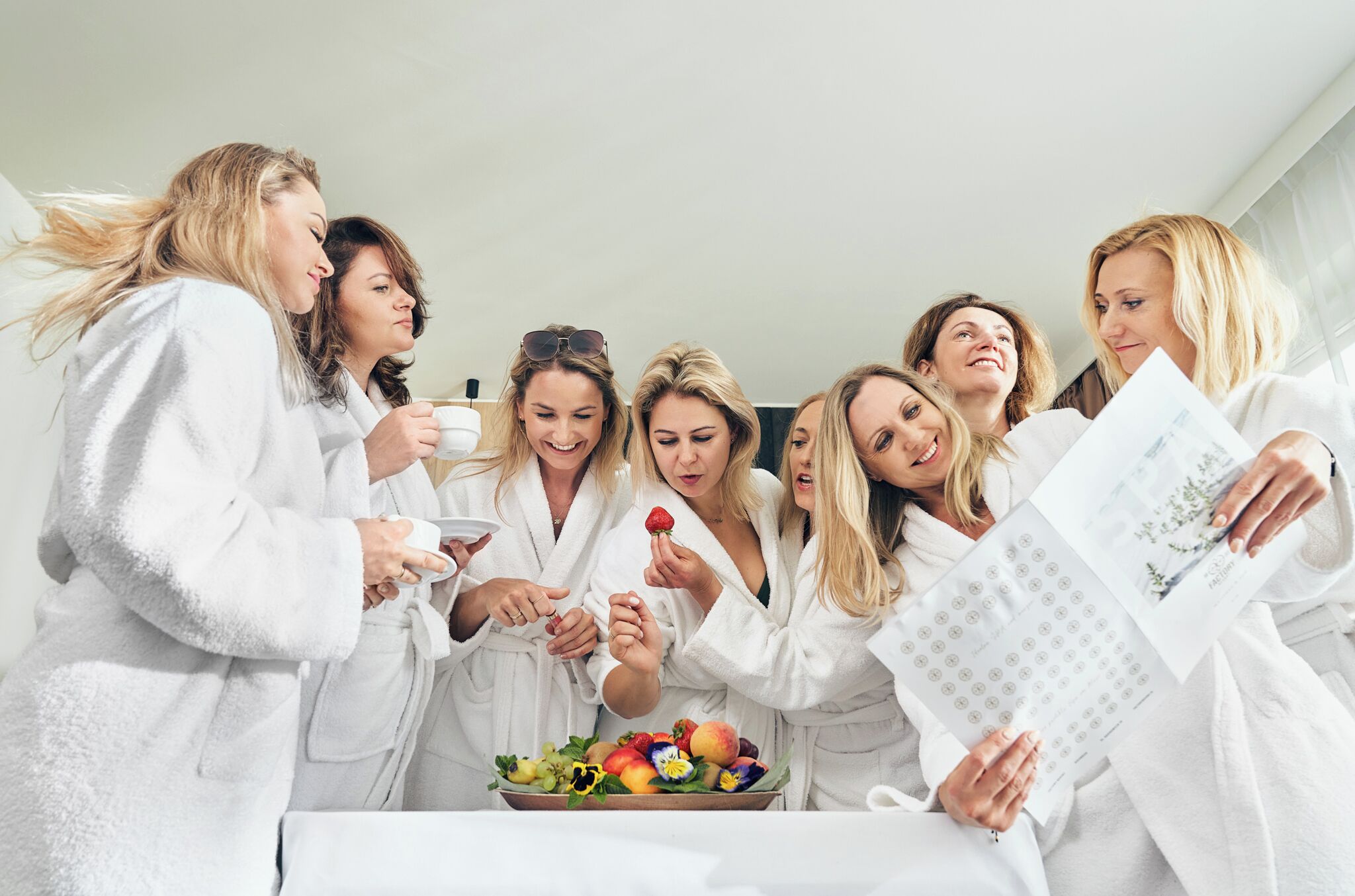 Um grupo de pessoas vestidas de branco reunido em volta de uma mesa com um prato de frutas e um cardápio.
