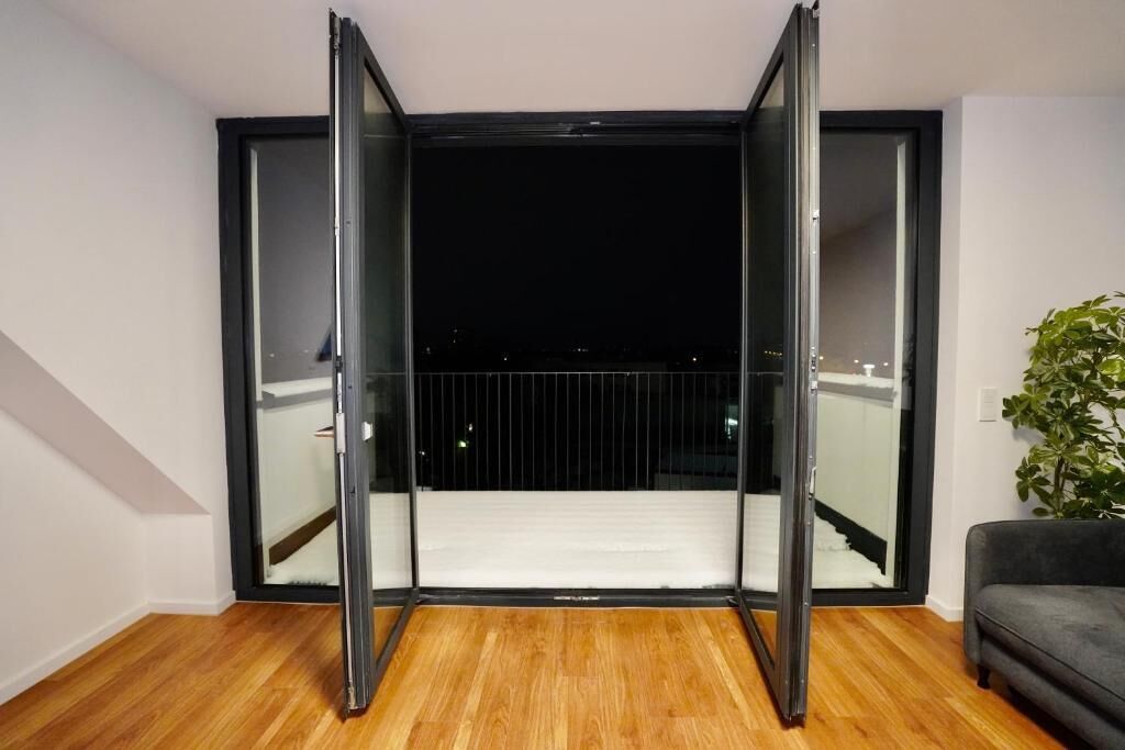 Quarto com porta de vidro deslizante que dá para uma varanda com vista para o céu noturno e as luzes da cidade.