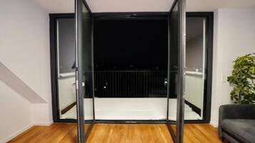 Quarto com porta de vidro deslizante que dá para uma varanda com vista para o céu noturno e as luzes da cidade.