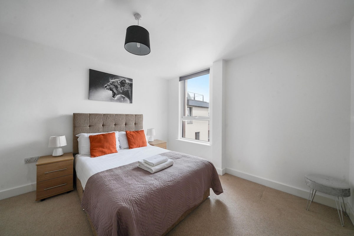 Quarto moderno com uma cama grande, uma mesa de cabeceira, uma luminária na parede, uma janela com vista e uma luminária no teto.