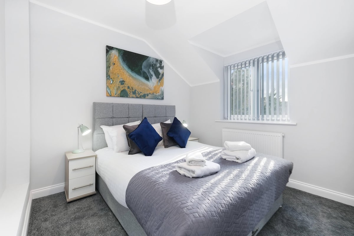 Um quarto moderno com uma cama grande, uma mesa de cabeceira, uma janela com persianas e um quadro na parede.
