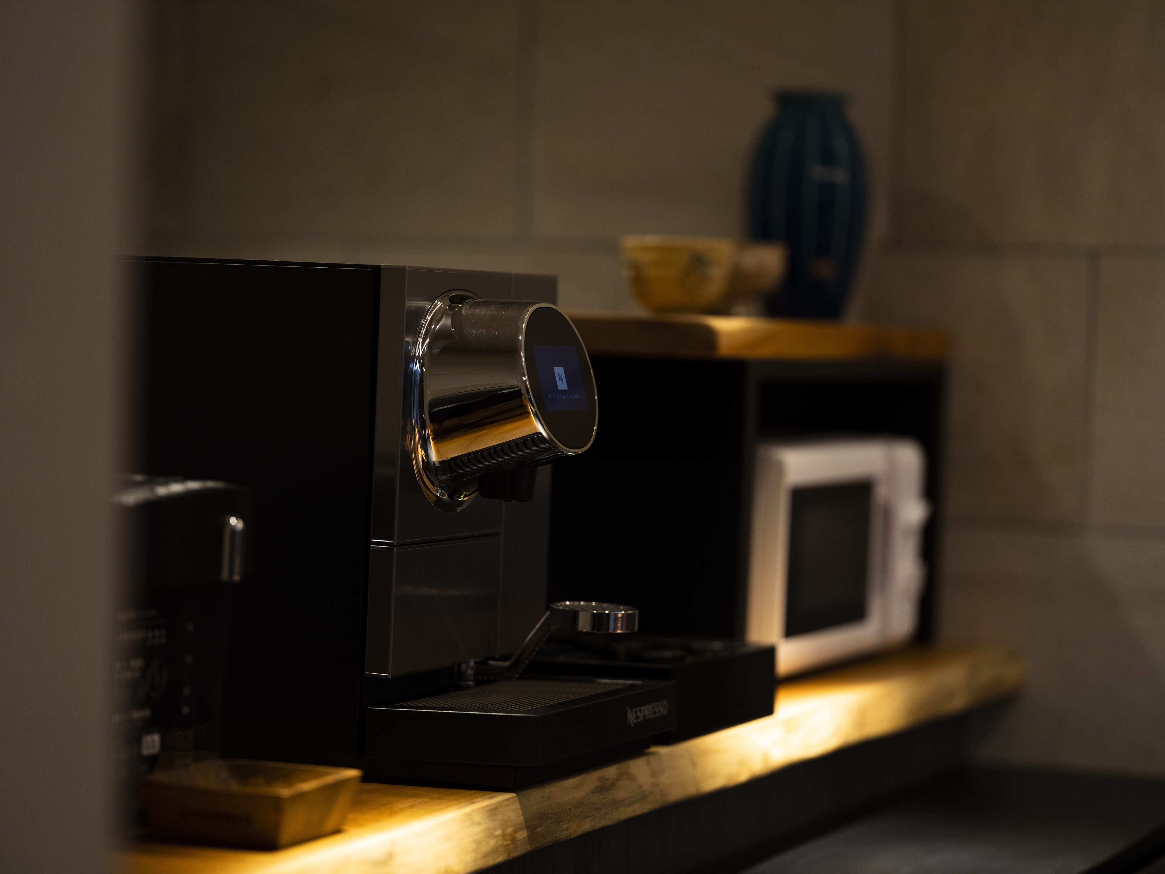 Máquina de café em bancada com micro-ondas ao fundo.