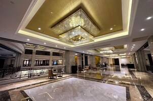 Um hall amplo com um grande candelabro, piso de mármore e diversas áreas de estar.