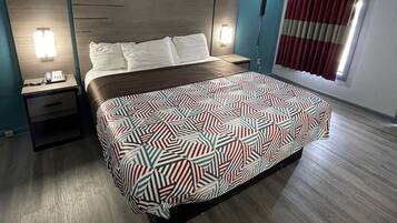 Quarto de hotel com cama, duas mesas de cabeceira, um criado-mudo, janela com cortinas e uma luminária fixada na parede.