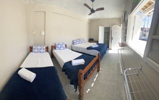 Quarto com três camas de solteiro, ventoinha no teto e vista para o exterior.