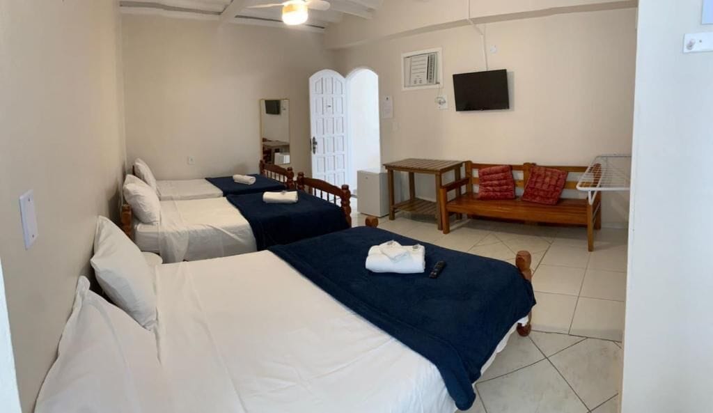 Quarto com duas camas, uma mesa pequena, uma cadeira, uma televisão e um guarda-roupa.