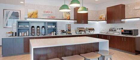 Uma cozinha moderna com uma ilha central, banquetas de bar e diversos eletrodomésticos.