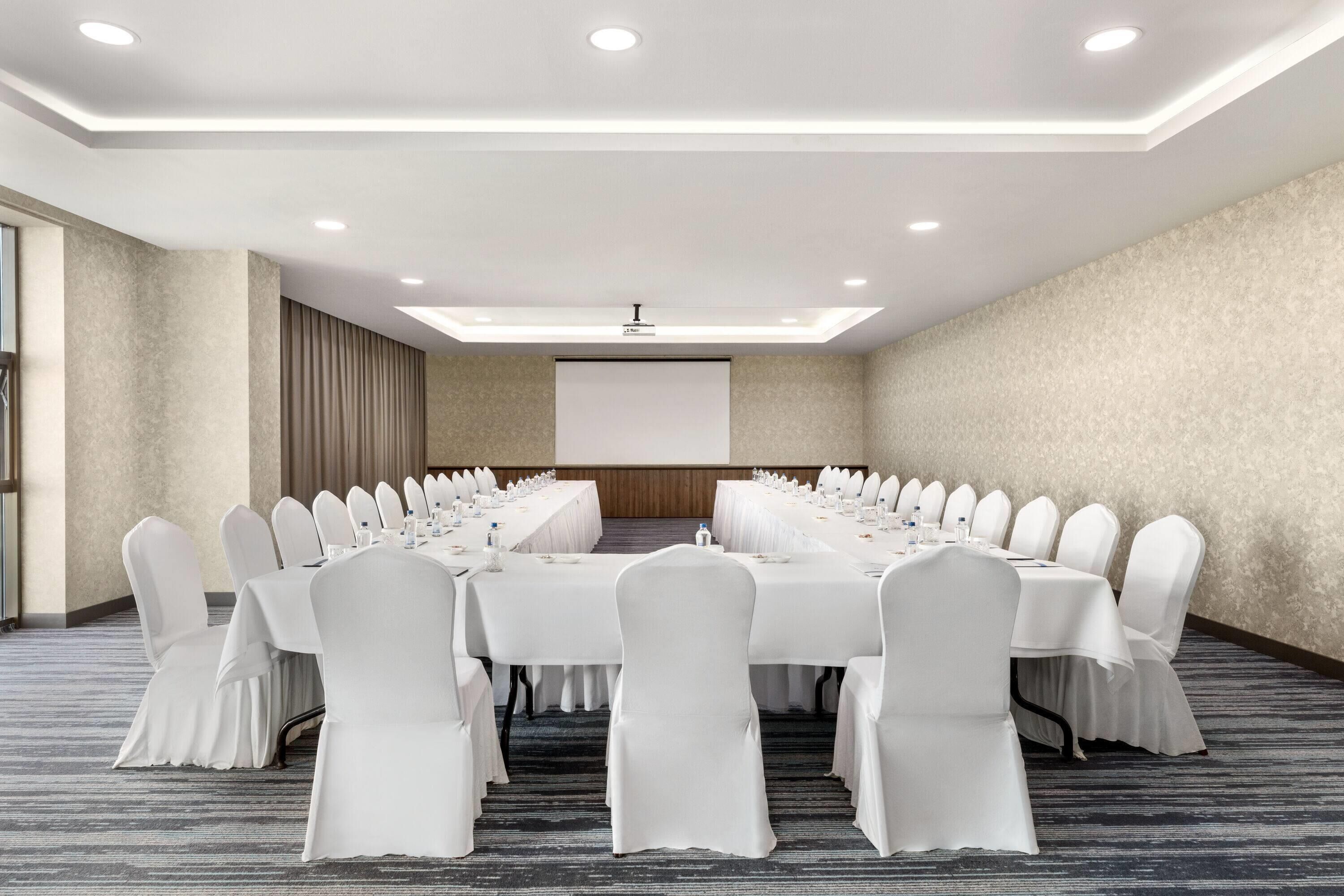Uma sala de conferências com uma mesa comprida, cadeiras e uma tela de projeção.