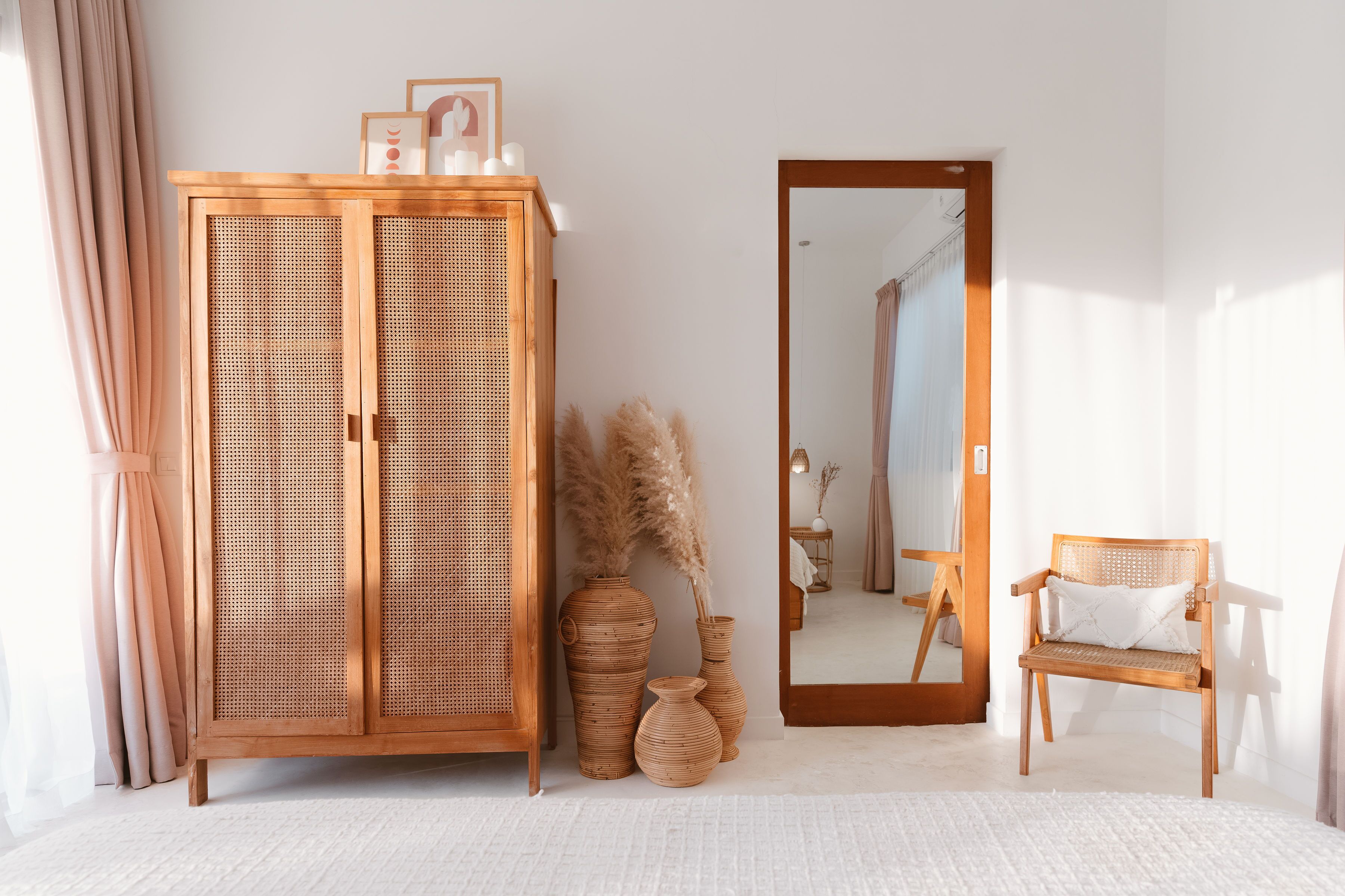 Quarto com guarda-roupa de madeira, espelho, cadeira de vime e uma pequena mesa com um vaso.