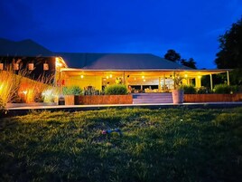 Um edifício moderno com área externa coberta, possivelmente um restaurante ou lounge, com entrada bem iluminada e um gramado à frente.