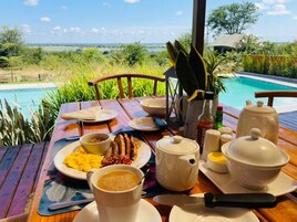 Uma mesa de jantar com itens de café da manhã, vista para uma piscina e vegetação exuberante.